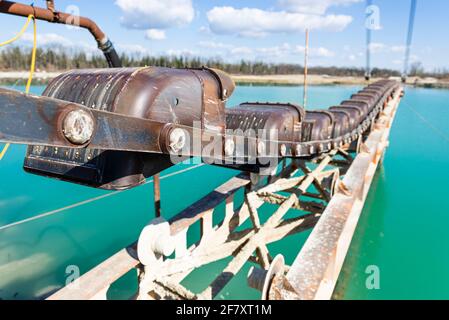 Ausleger mit Baggerschaufeln an einem orangenen Kiesbagger an einem ...