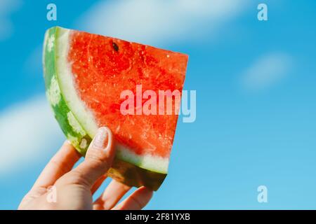 fresh red watermelon slice held by hand with ripe watermelon on wooden ...