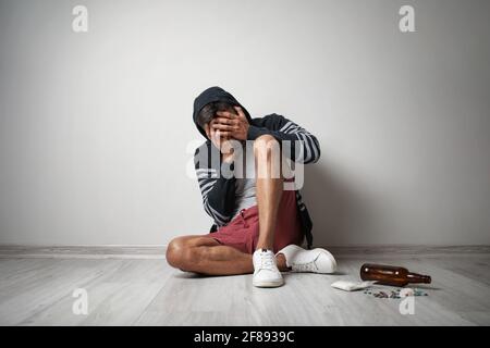 Male junkie with drugs and alcohol sitting on floor Stock Photo - Alamy