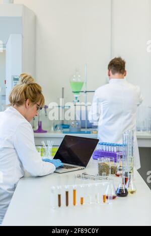 Wide shot of female chemical scientist working on laptop in laboratory ...