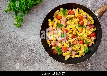 Colorful pasta rotini, cherry tomatoes and ham on pan. Close up. Top ...