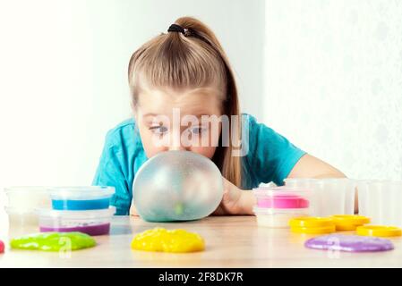A blonde child blows a slime bubble. Play a slime toy. Making slime at ...