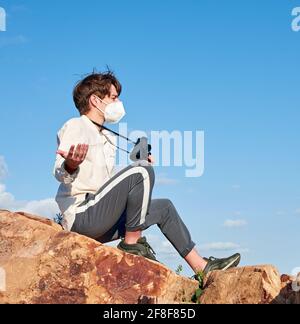 Side view of an explorer from Spain in a mask sitting on a rock in the ...
