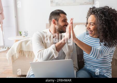 pleased interracial couple smiling near funny shiba inu dog in kitchen ...