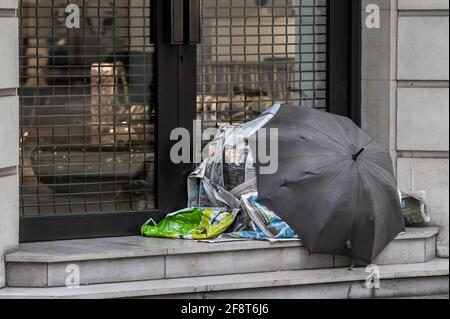A person sleeps under an umbrella next to piles of books stacked on a ...