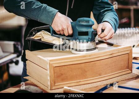 A man using an orbital wood sander in a workshop. Close-up of a ...