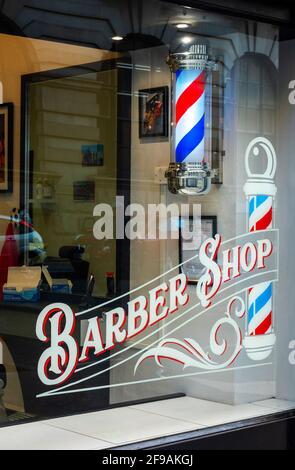 A red, white, and blue barber pole is mounted on the exterior wall of a ...