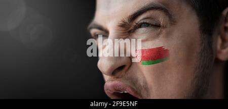 A screaming man with the image of the Belarus national flag on his face ...
