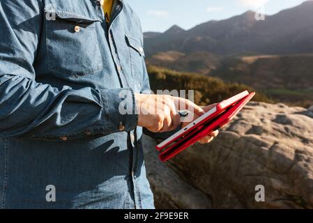Tranquil male explorer with tablet sitting on hill in mountainous ...