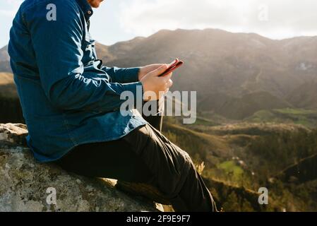 Tranquil male explorer with tablet sitting on hill in mountainous ...