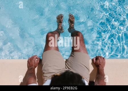 Top view of male freelancer sitting at poolside with legs in water ...