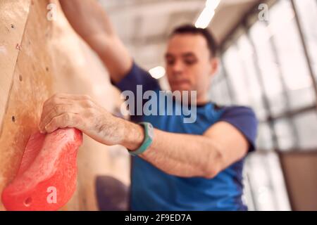 Low angle of muscular male alpinist hanging on climbing wall while ...