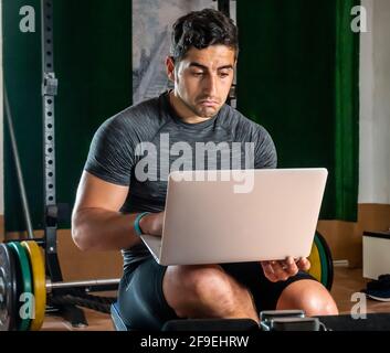 Latino coach in sportswear working out in gym with computer preparing ...