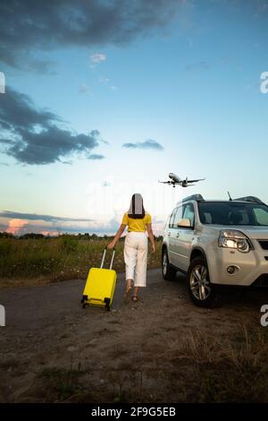 woman with luggage near white suv car plane in the air. copy space ...