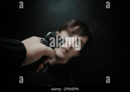 First person view of gun aimed at young man on dark background. POV of ...