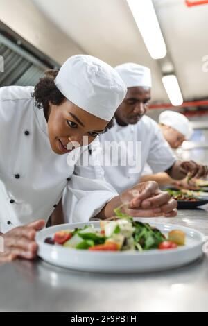 Mixed race professional chef finishing dish before serving with ...
