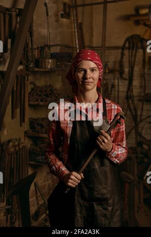 Positive young female blacksmith in uniform and gloves smiling and ...
