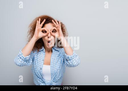 young curly woman imitating eyeglasses with hands and sticking out ...