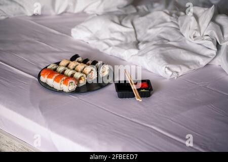 A plate with a sushi set stands on a white bedspread, rolls for a ...