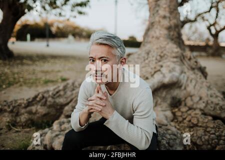 Man sitting on tree roots in woods Stock Photo - Alamy