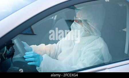 Unidentifiable person in protective overall suit driving car. Car side ...