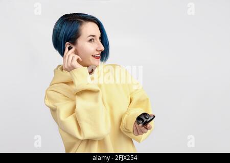 A female in yellow hoody holding wireless earphones. The white ...