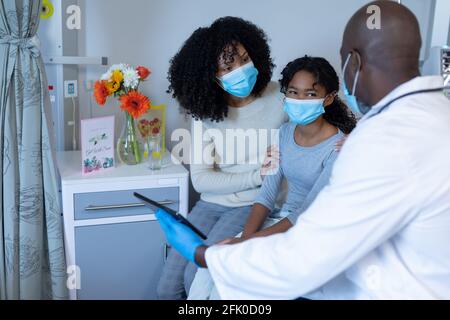 Diverse mother, ill daughter and male doctor sit on hospital bed using ...