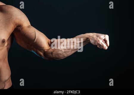 tense arm clenched into fist, veins, bodybuilder muscles on a dark ...