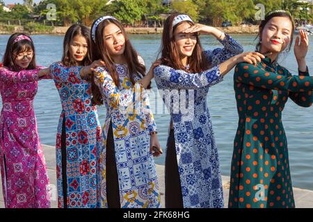 Group of pretty Vietnamese females wearing traditional Ao Dai posing by the riverside in the old ...