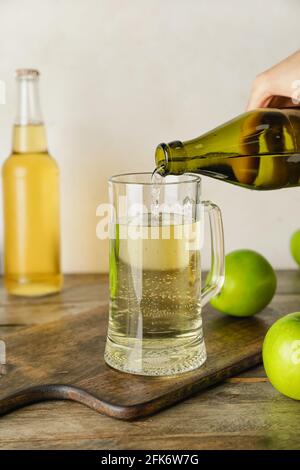 Woman pouring cold cider from bottle into glass on wooden background ...