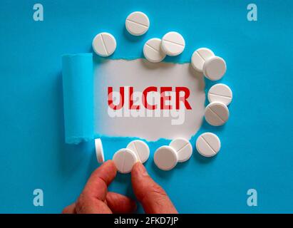 Stomach ulcer symbol. The word 'ulcer' appearing behind torn blue paper ...