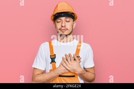 Hispanic young man wearing handyman uniform looking away to side with ...