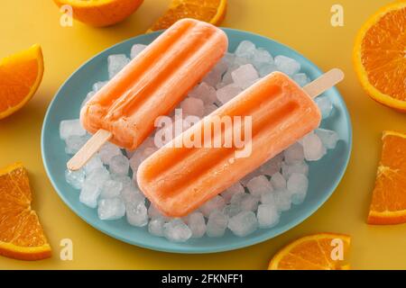 Orange popsicles on blue plate on yellow background Stock Photo - Alamy