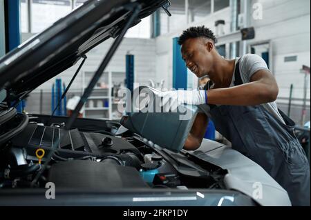 Male worker changes oil in engine, car service. Vehicle repairing ...