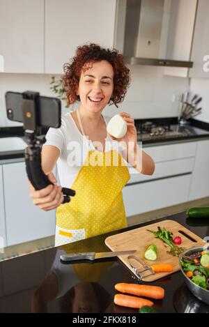 Woman youtuber records herself with her smartphone in her kitchen while ...