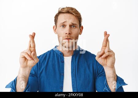 Hopeful sad man making a wish, cross fingers for good luck and sulking ...