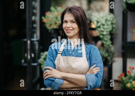 Young woman seller in apron stands in trading hall with box of apples ...