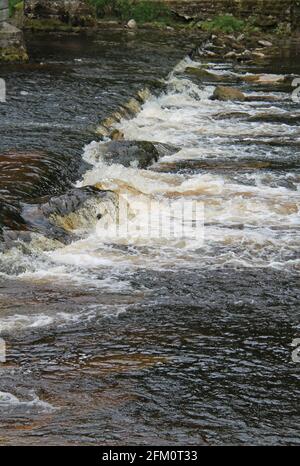 A wide but shallow river flowing in the shadow of a high mountain ...