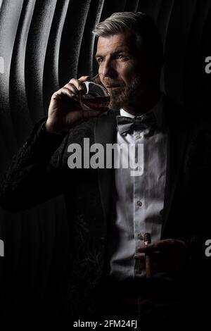 Portrait of a mature mafia man drinking and smoking while sitting at ...