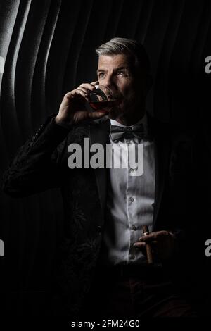 Portrait of a mature mafia man drinking and smoking while sitting at ...