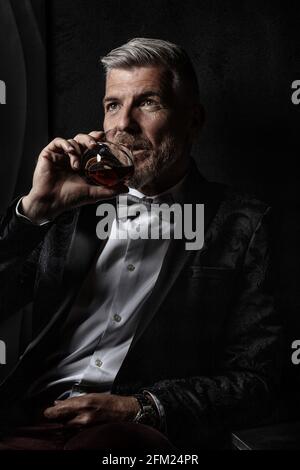 Portrait of a mature mafia man drinking and smoking while sitting at ...