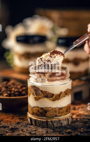 Portion of Classic tiramisu dessert in a glass cup on dark concrete ...