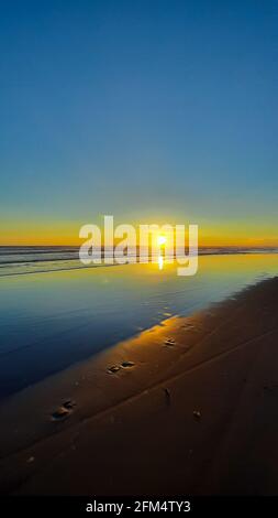 Wide wet sand beach reflecting orange sunlight while sunset Stock Photo ...