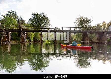 Woman kayaking to wooden bridge over the river Krka in Slovenia, with ...