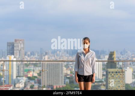 An Asian female wearing a protective face mask buying clothes in a ...