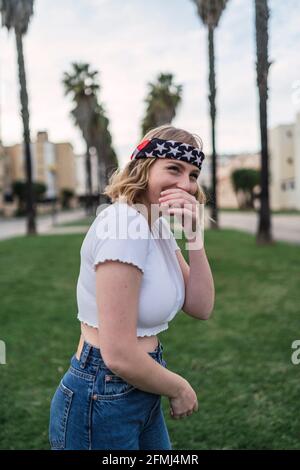 Laughing young woman with USA flag pointing at something on green ...