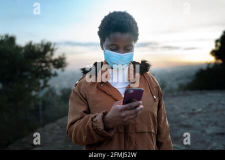 African American female traveler with protective mask using cell phone ...
