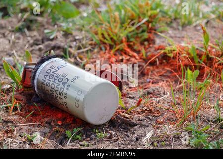 a discharged British Army red smoke grenade lying on mud and grass ...