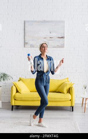 Smiling housewife in headband holding digital tablet on yellow ...