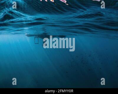 Underwater view of a boat bottom part and fishes swimming in clear blue ...